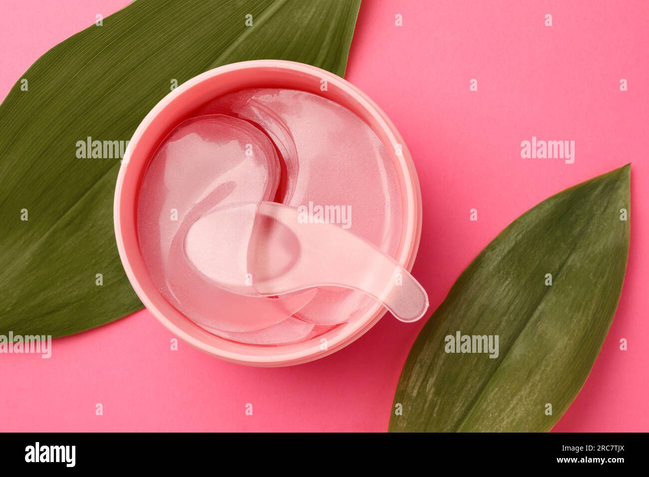 Jar of under eye patches with spoon and green leaves on pink background ...