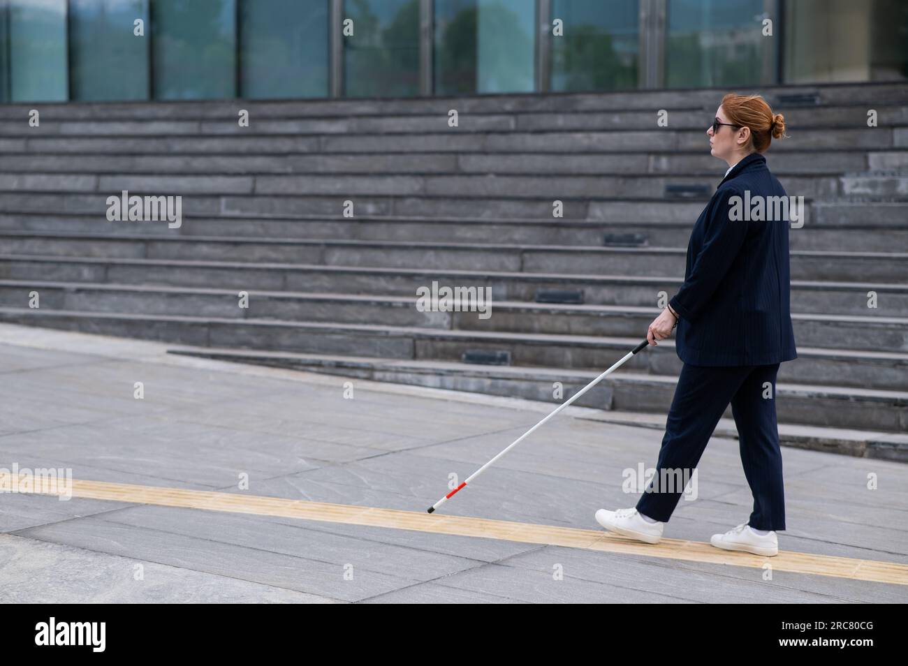 Blind businesswoman walking along tactile tiles with a cane Stock Photo ...