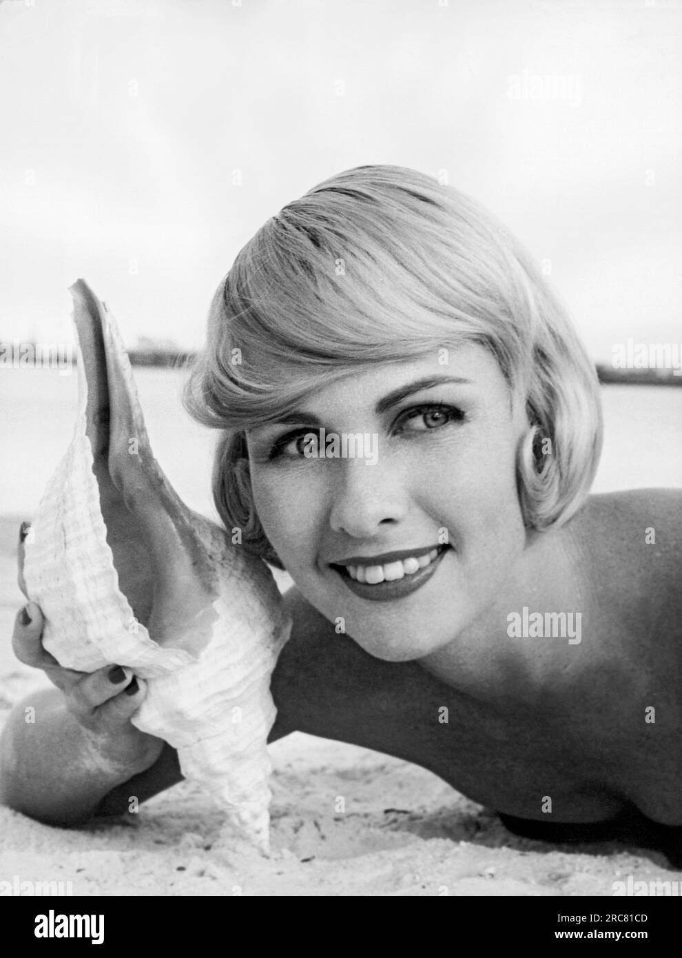 United States: c. 1962. A pretty blond woman lies on the beach with a ...