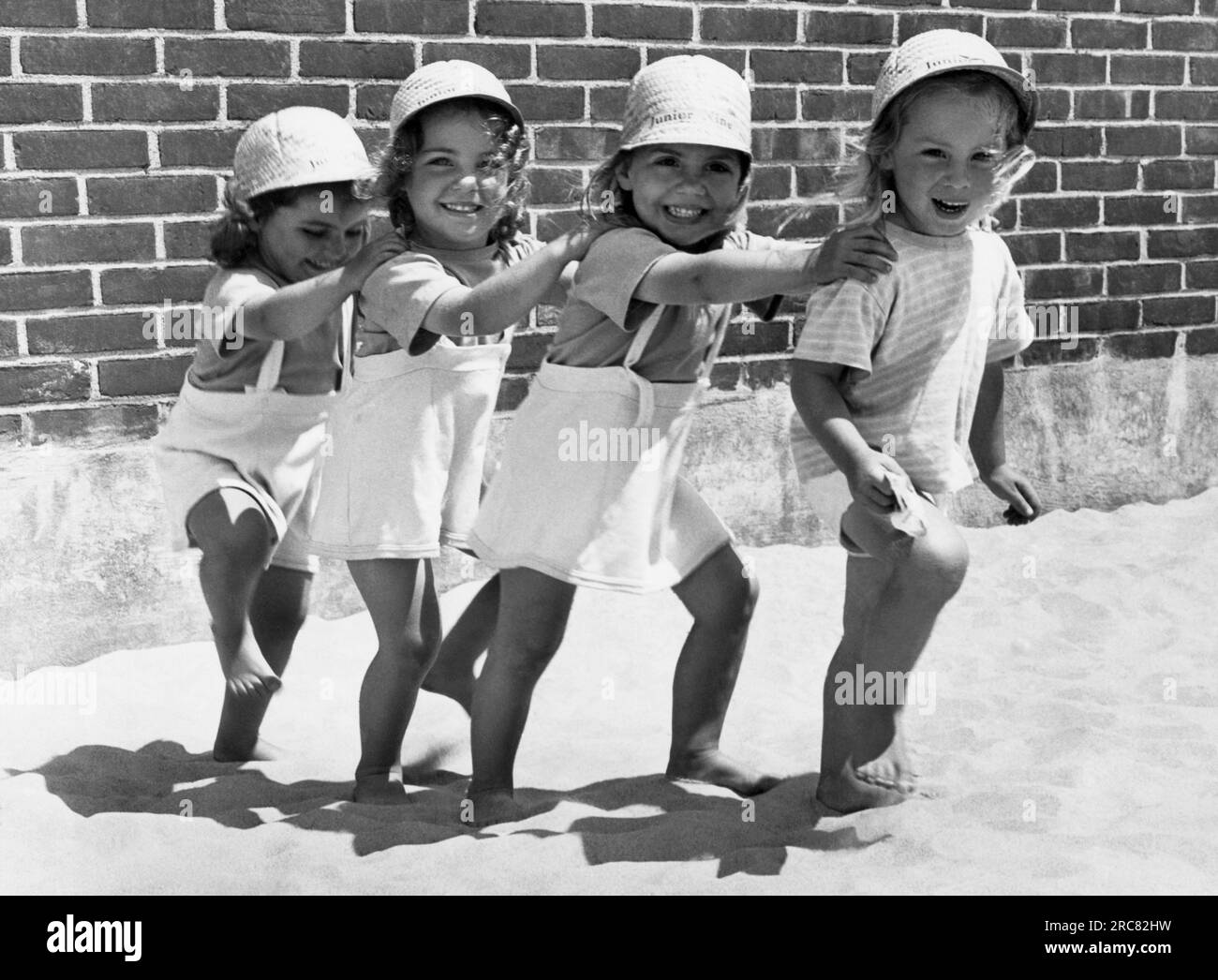 United States: 1952 Four little girls marching across the sand in their ...