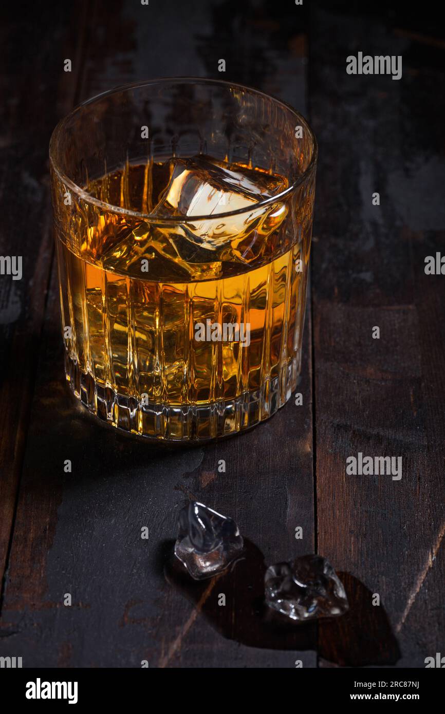 Single malt scotch whiskey in crystal glass with ice cubes on wooden table background. Top view ...