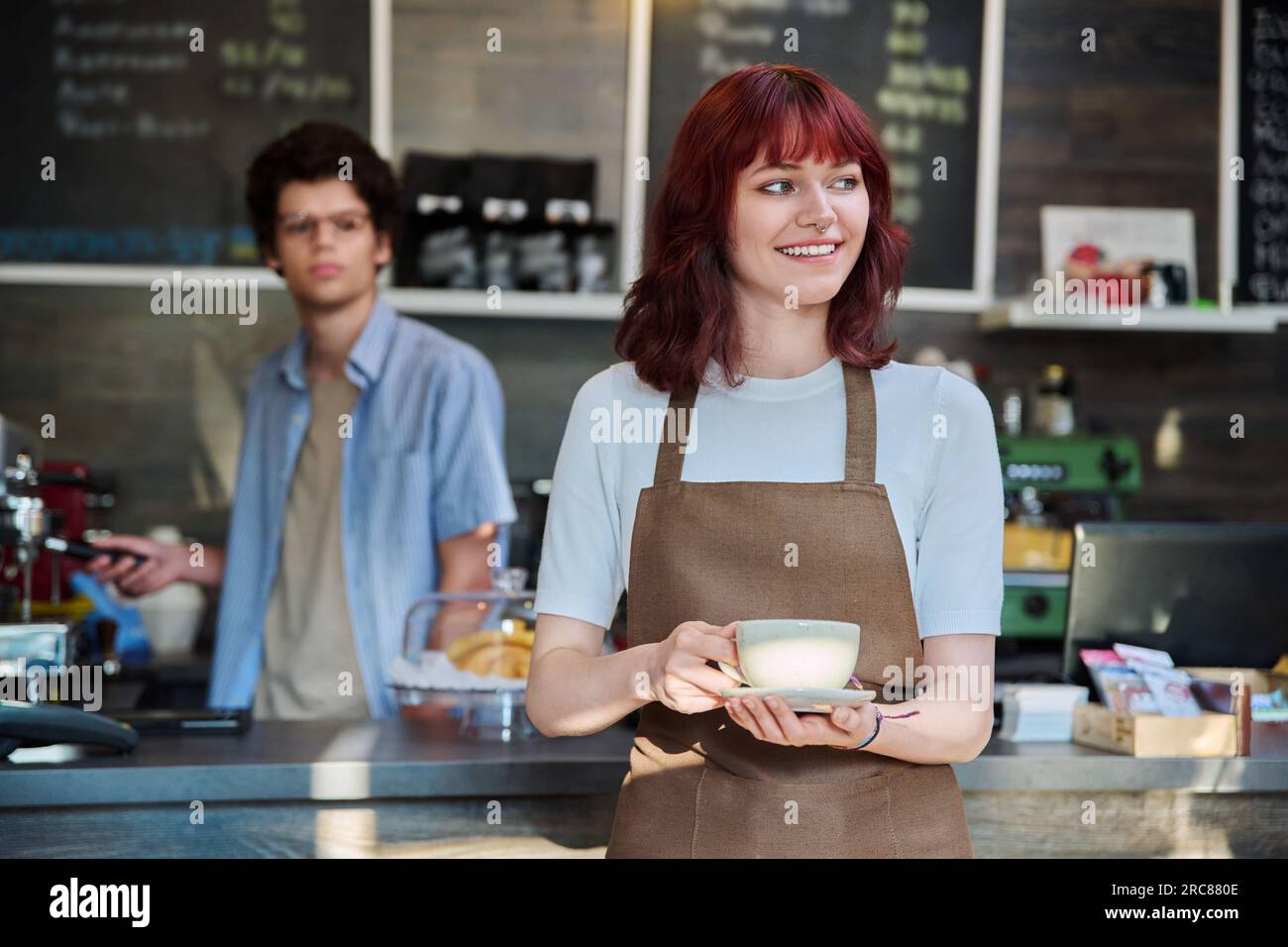 Portrait of young female waitress in front of counter in coffee shop ...