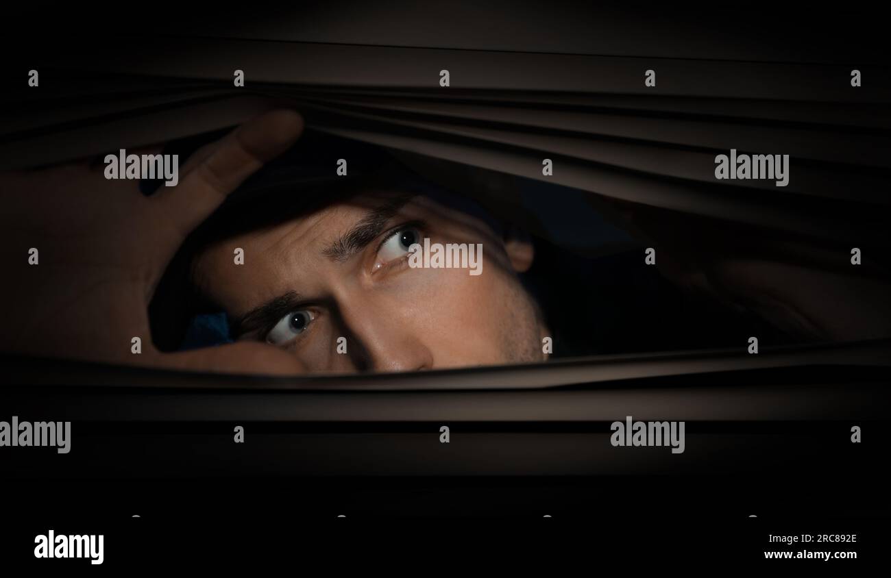 Worried man looking through window blinds into darkness. Paranoia ...
