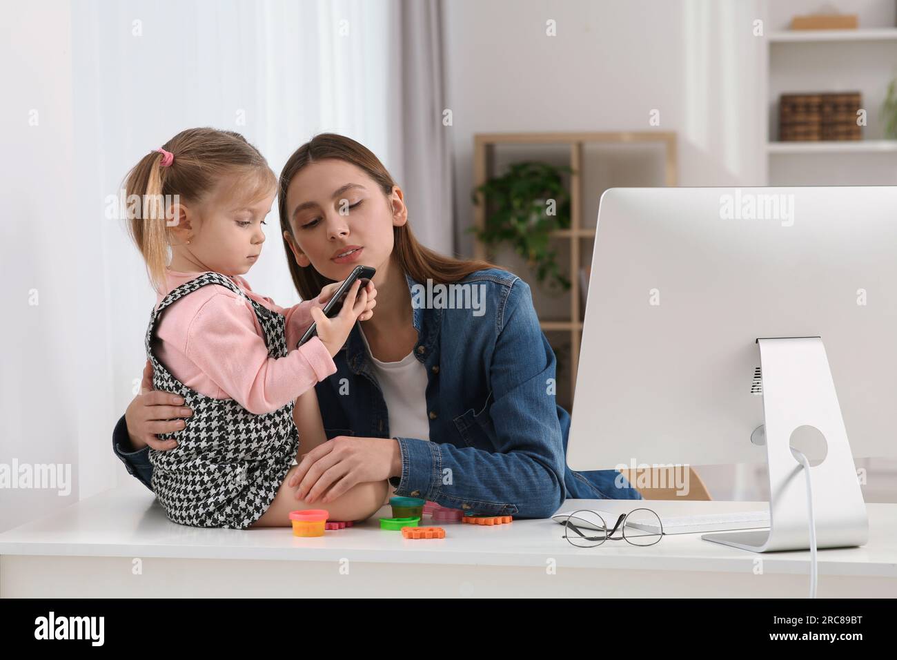 Mother spending time with her daughter at home. Child sitting on desk ...