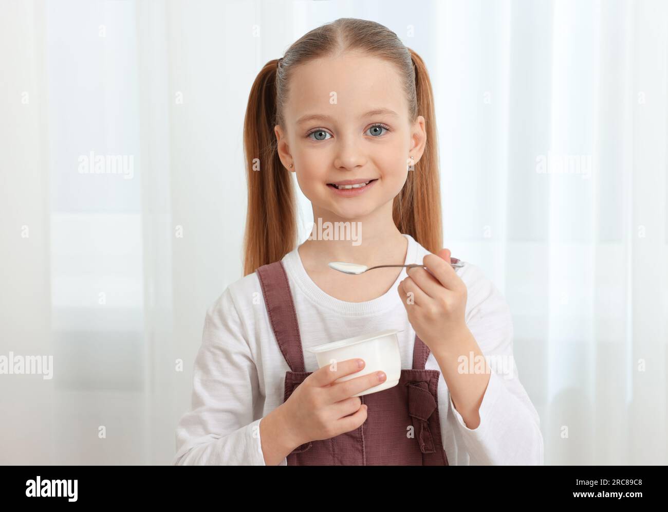 Cute little girl with tasty yogurt indoors Stock Photo - Alamy