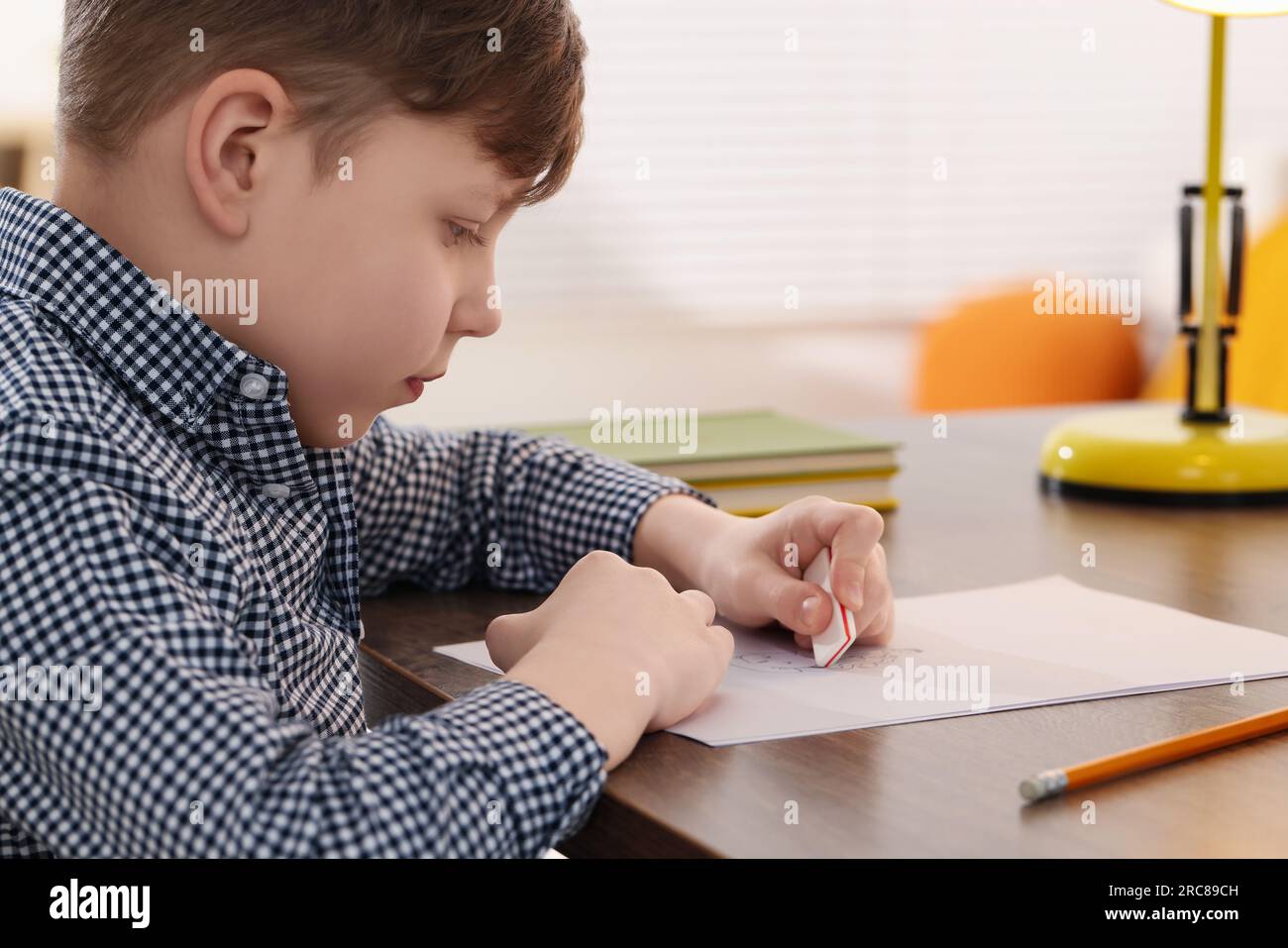 Little boy erasing mistake in his notebook at wooden desk indoors Stock ...