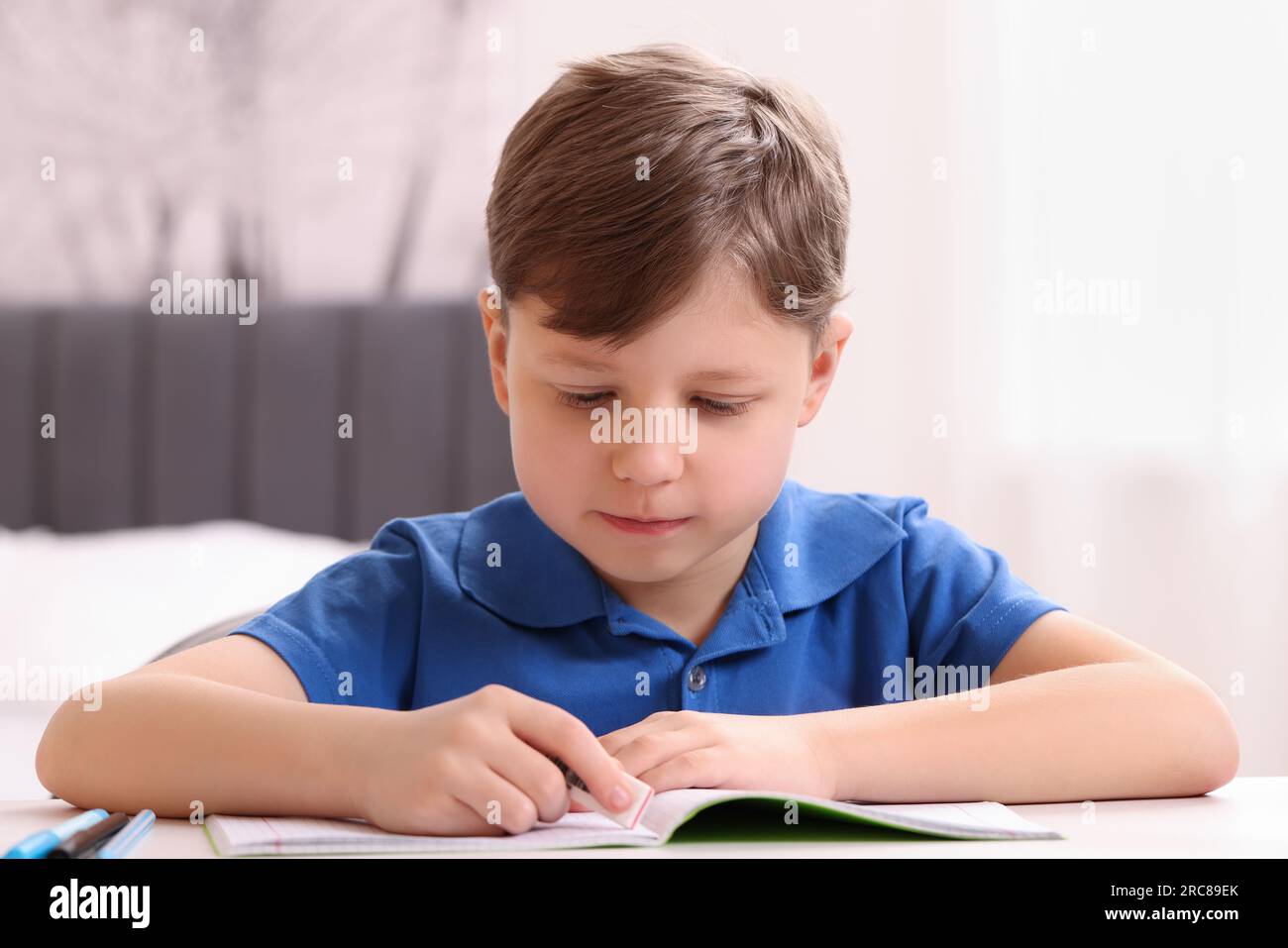 Little boy erasing mistake in his notebook at white desk indoors Stock ...