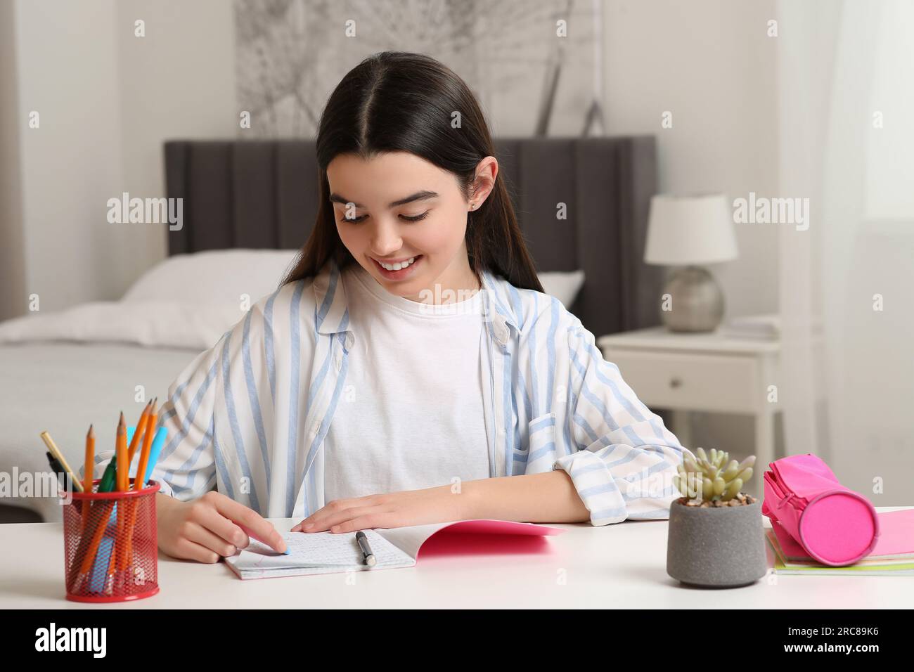 Teenage girl erasing mistake in her notebook at white desk indoors ...