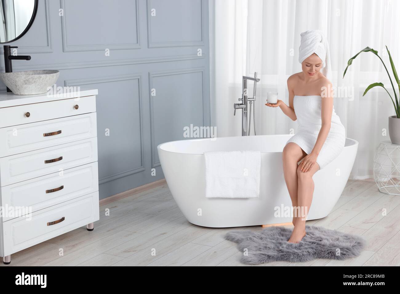 Beautiful young woman applying body cream onto leg in bathroom Stock ...