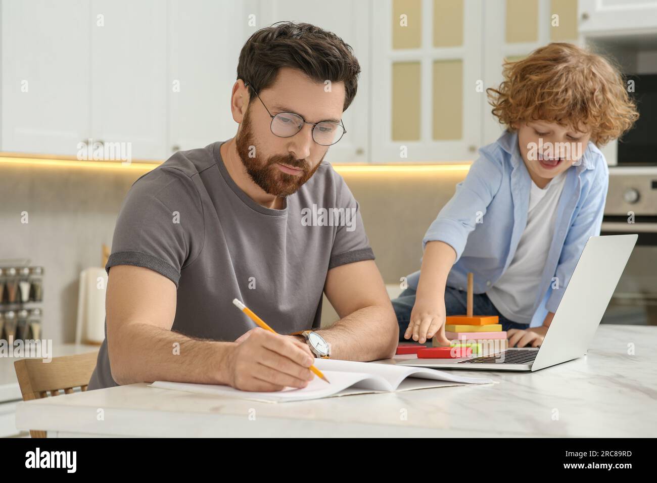 Father working remotely while his son playing with toys at home. Man ...