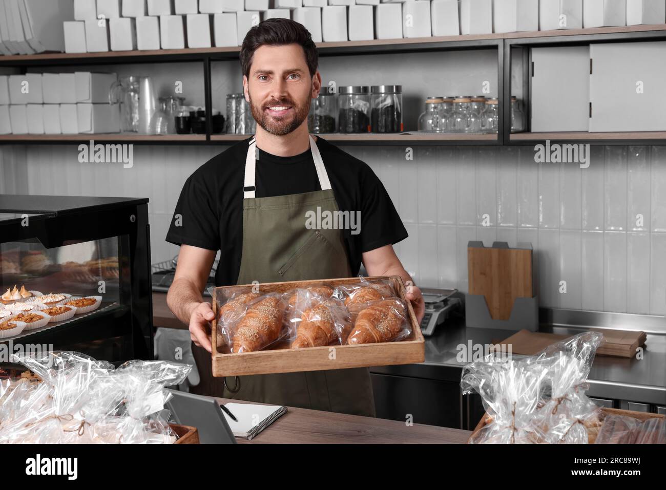 Happy seller with croissants at cashier desk in bakery shop Stock Photo ...