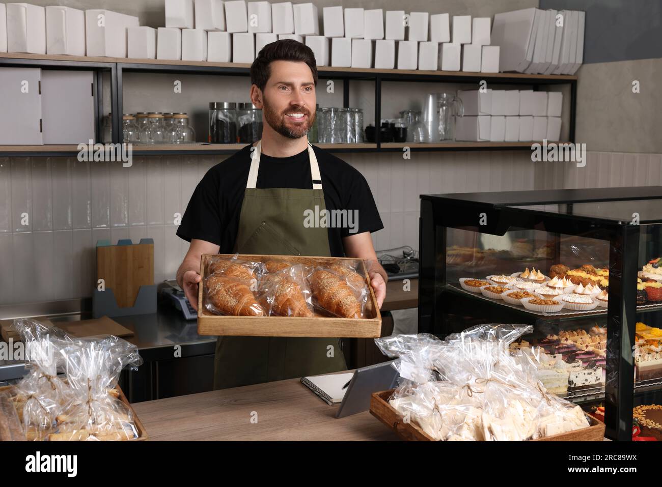 Happy seller with croissants at cashier desk in bakery shop Stock Photo ...