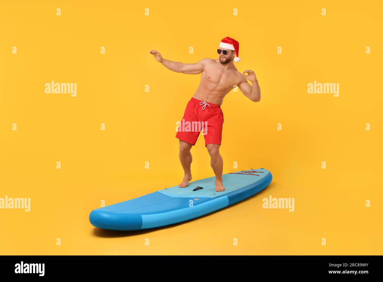 Happy man in Santa hat balancing on SUP board against orange background ...