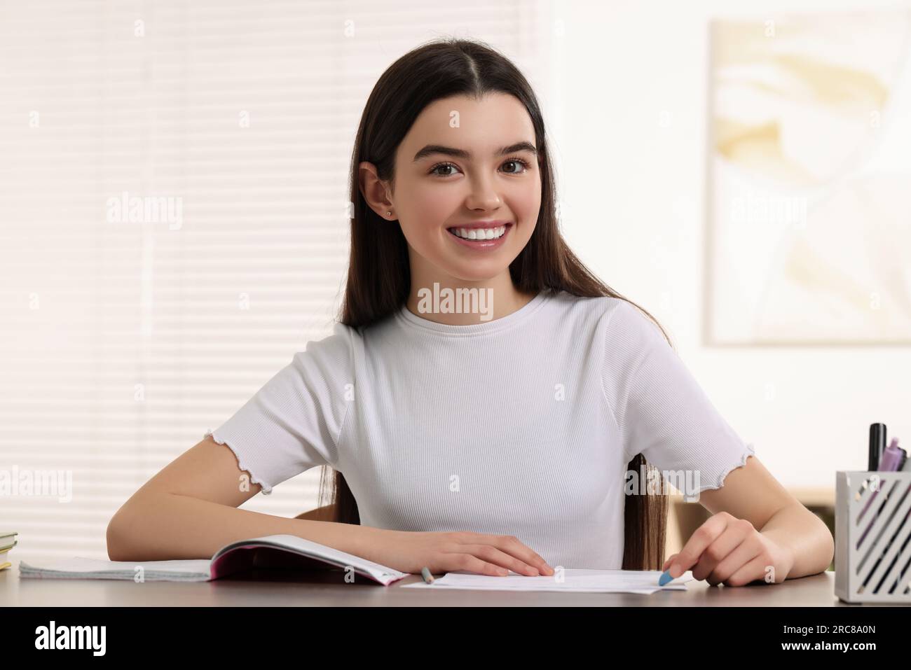 Teenage girl erasing mistake in her notebook at wooden desk indoors ...