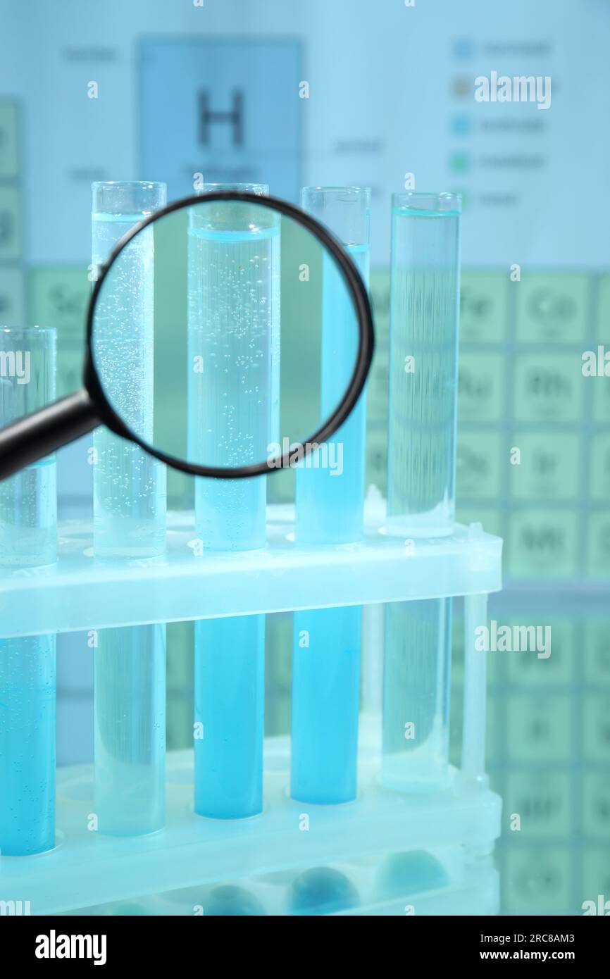 Magnifying glass and test tubes in rack on mirror surface against ...