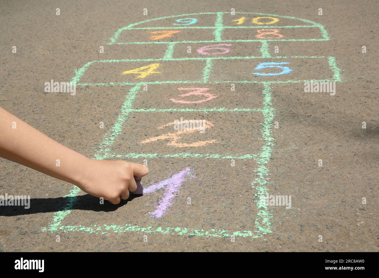 Child drawing hopscotch with colorful chalk on asphalt outdoors ...