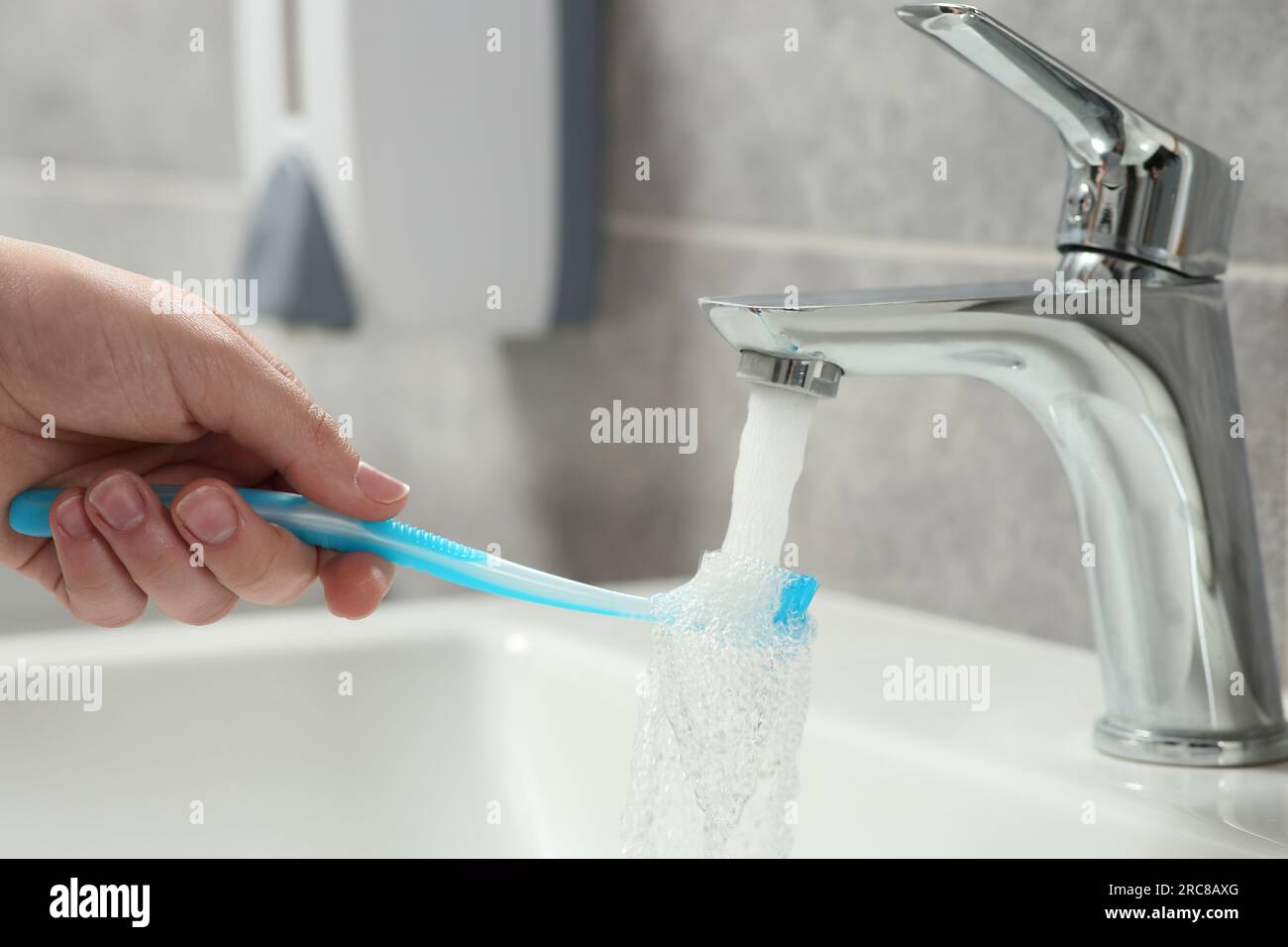 Woman washing plastic toothbrush under flowing water from faucet in ...