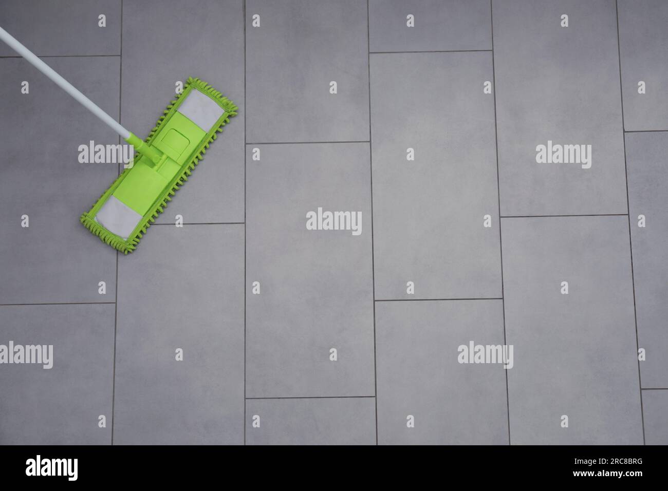 Cleaning grey tiled floor with microfiber mop, top view. Space for text ...