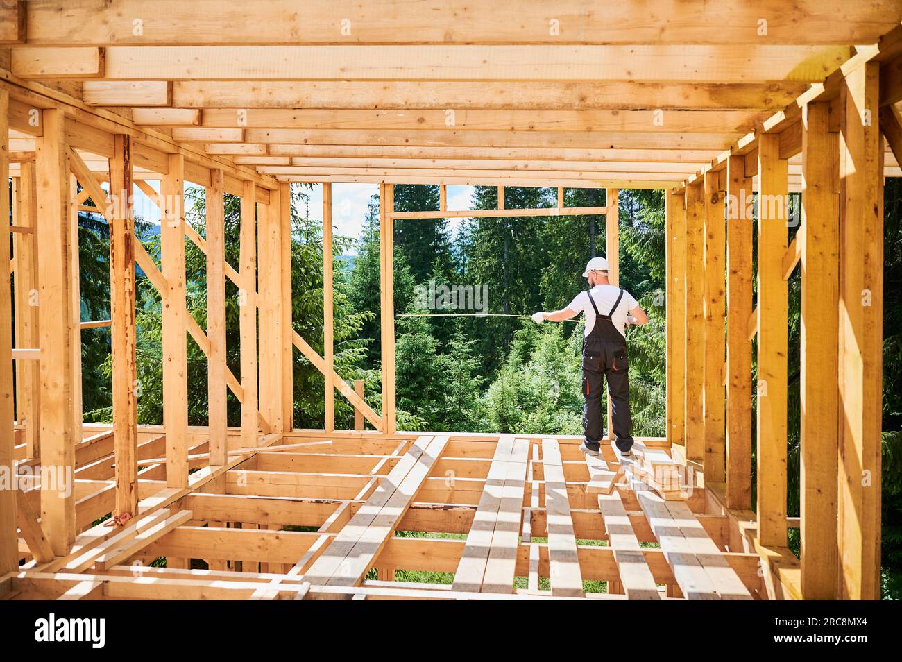 Carpenter is constructing wooden frame house. Back view of man taking ...