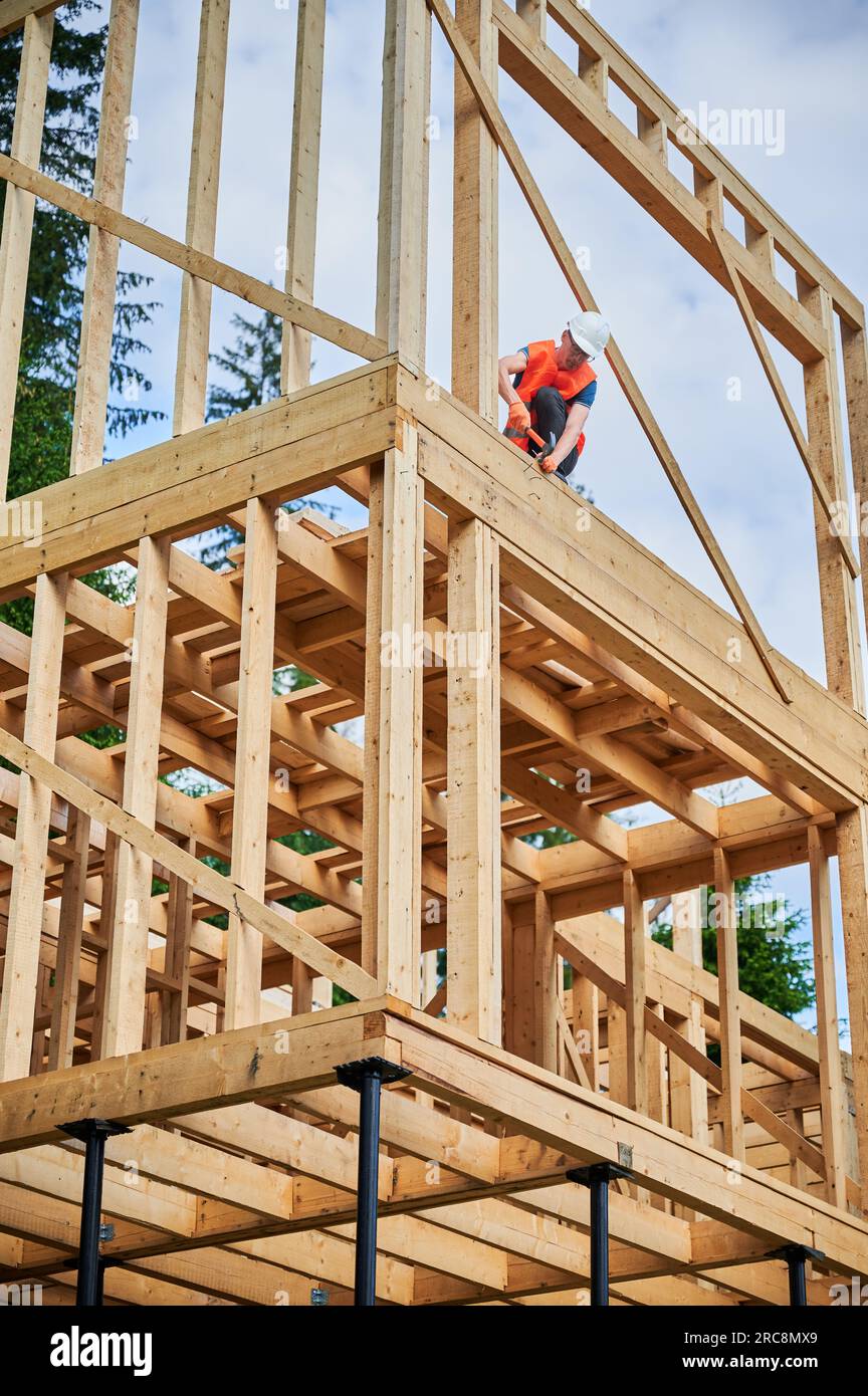 Wooden two-story frame house being built by carpenter. Man wearing ...