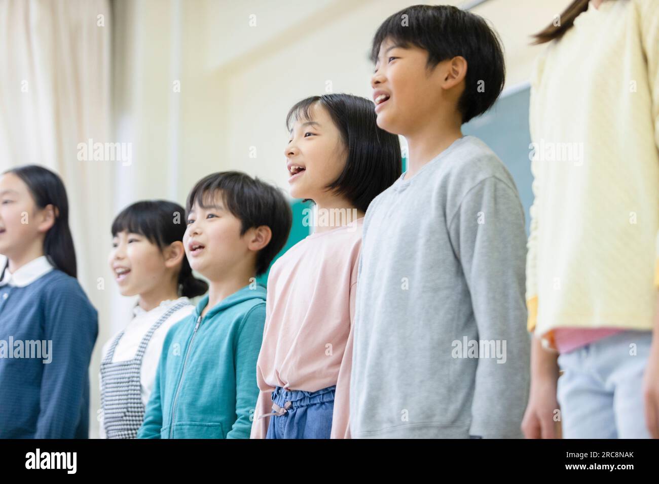 Elementary school students singing a song in front of the blackboard ...