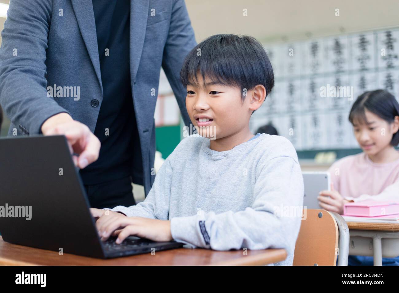 An elementary school student and his teacher studying with a notebook ...