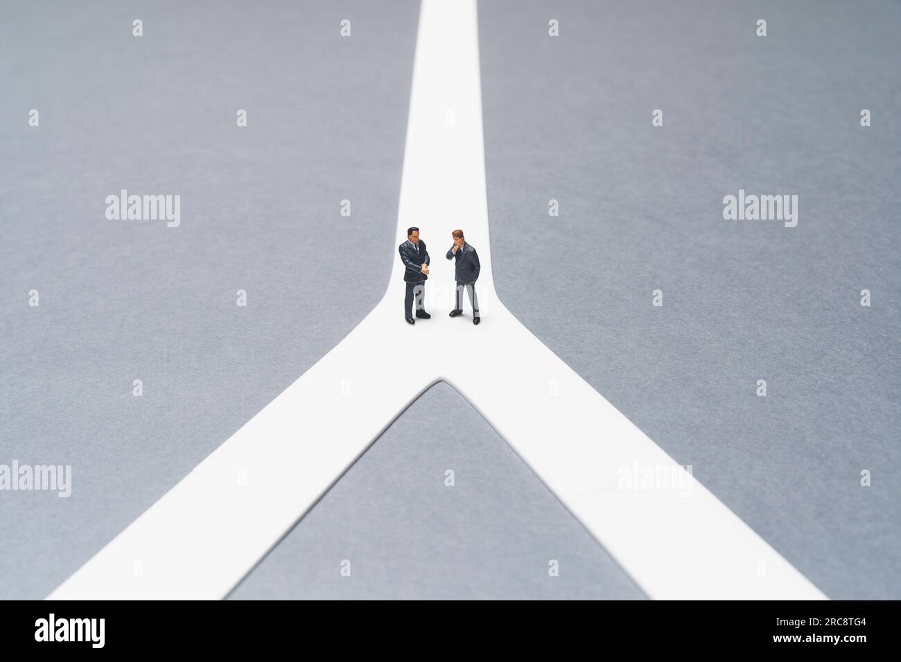 Miniature businessman having a meeting in front of a fork in the road ...