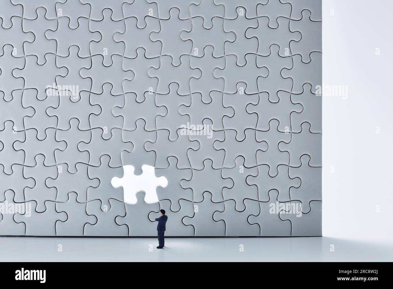 Miniature doll looking at the last empty piece of a white puzzle Stock ...