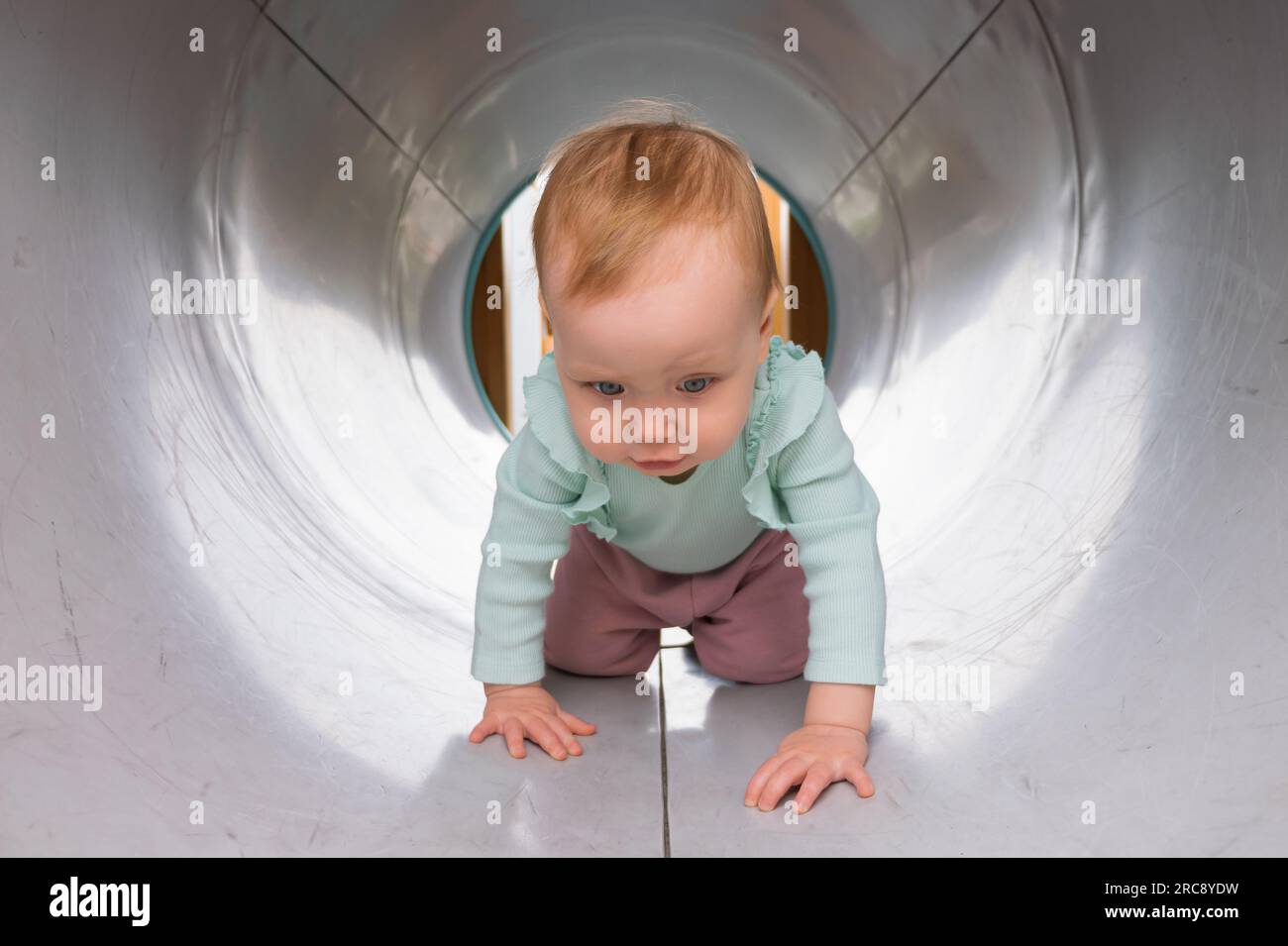 Toddler girl likes to crawl along gray pipe on playground Stock Photo ...