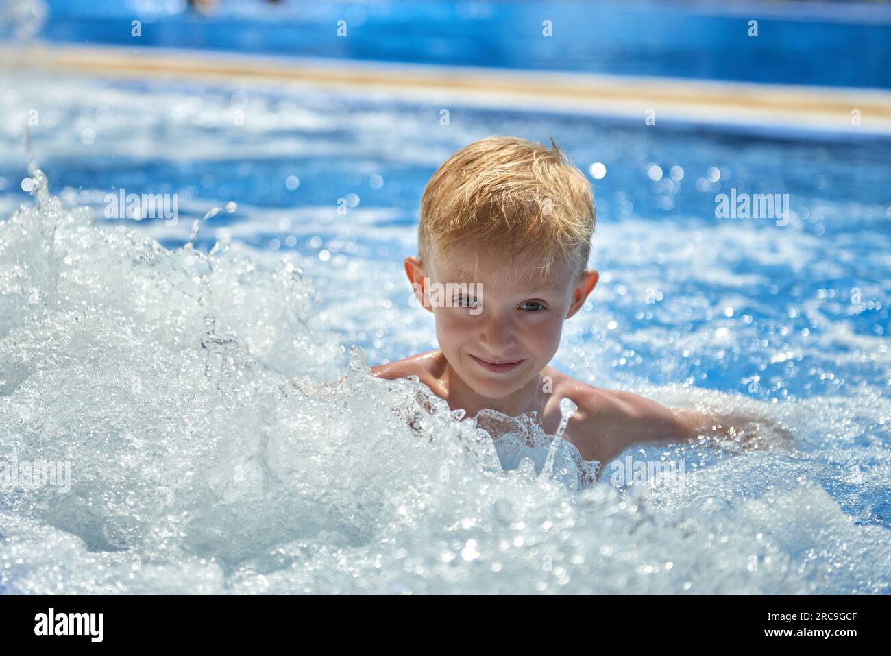 Young boy kid child eight years old splashing in swimming pool having ...