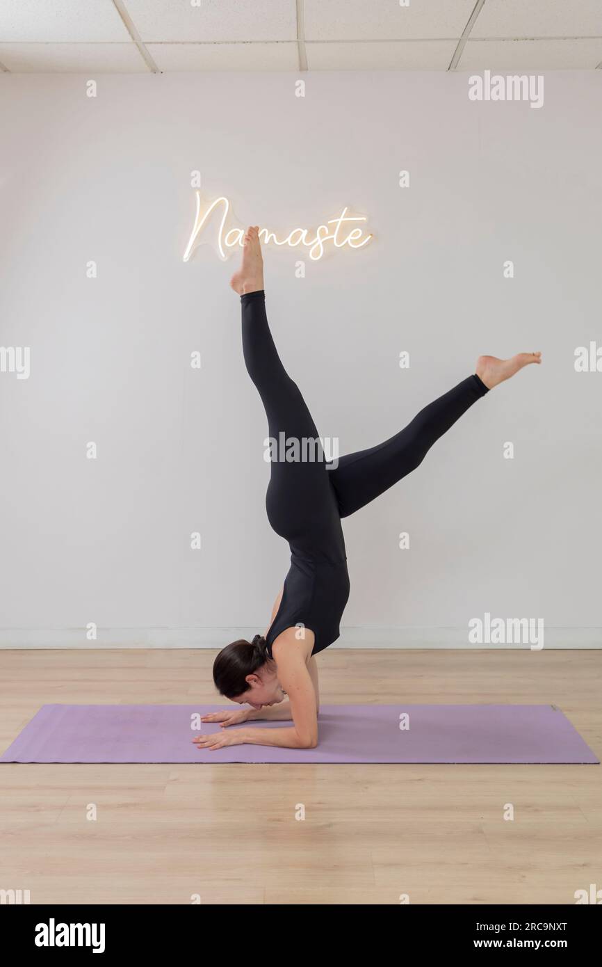 Young woman in sportswear practices yoga in a studio doing a handstand ...