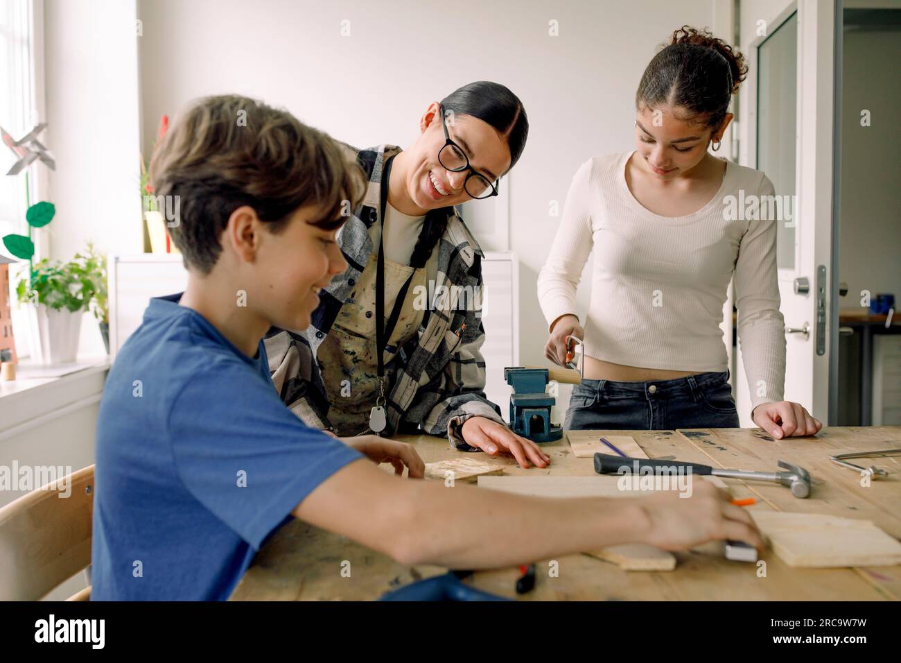 Smiling young teacher with male and female students during carpentry ...