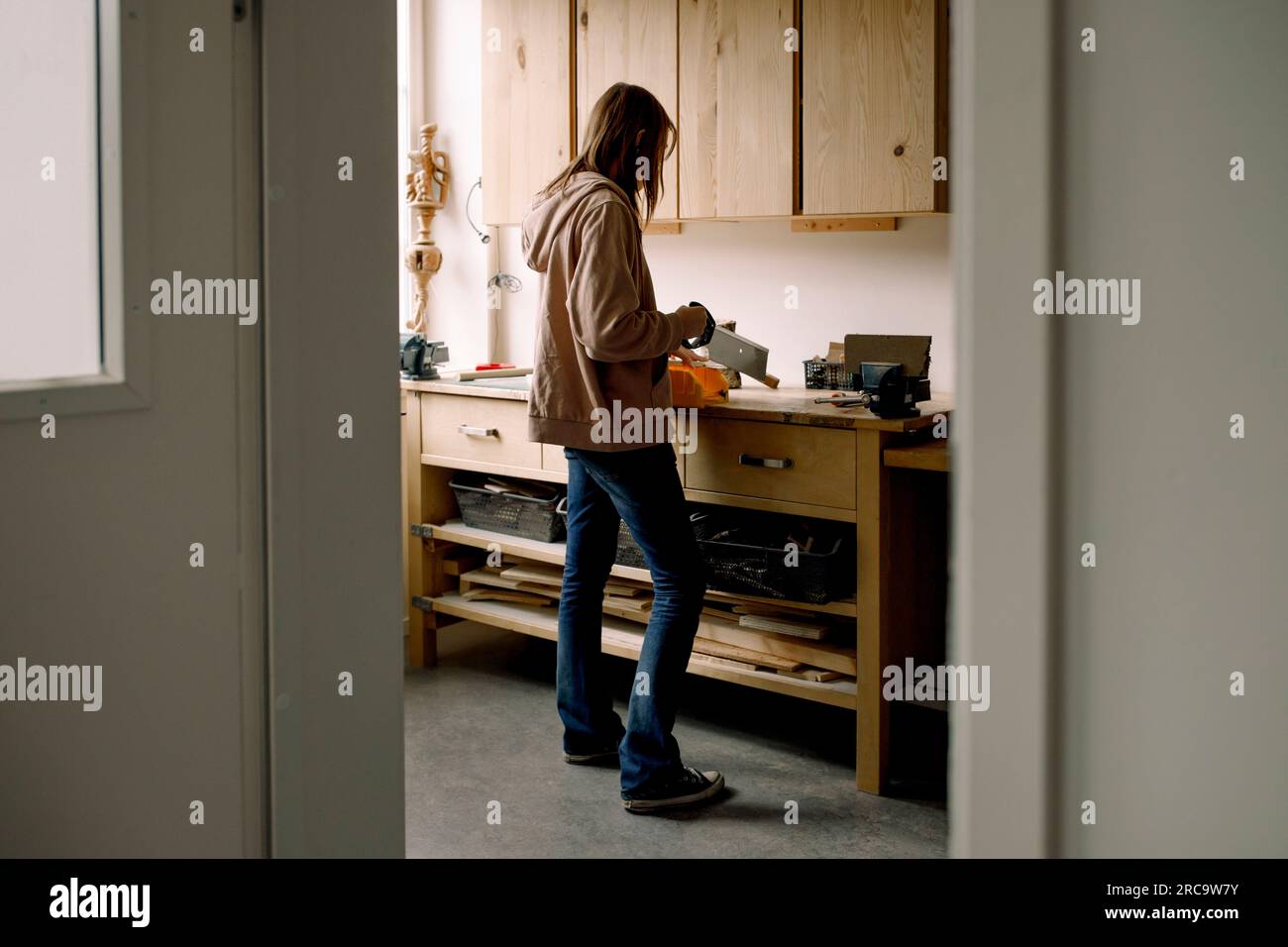 Female teenage student cutting wood during carpentry class seen through ...