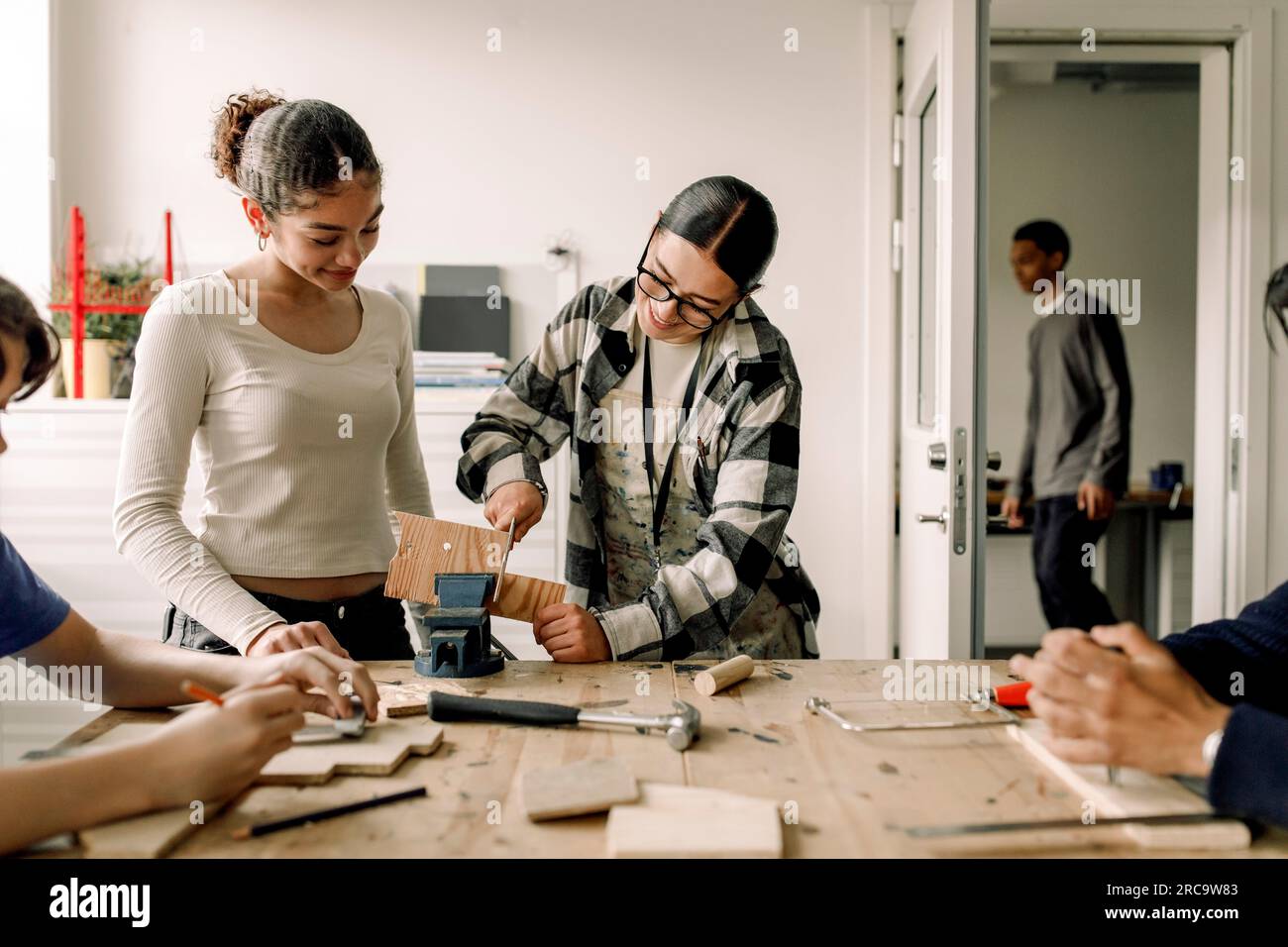 Teacher helping female teenage student while cutting wood during ...