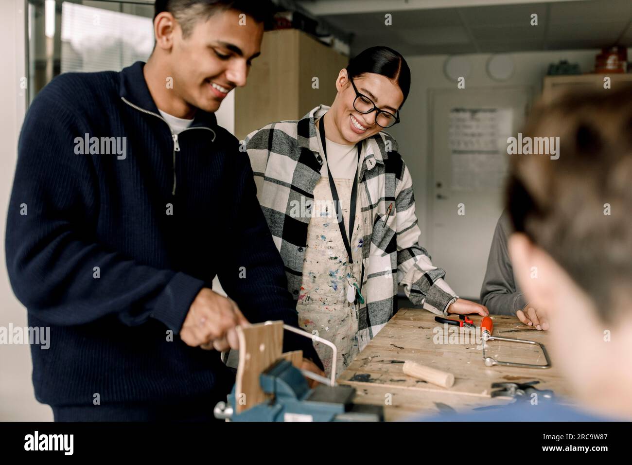 Happy female teacher standing with male student cutting wood during ...