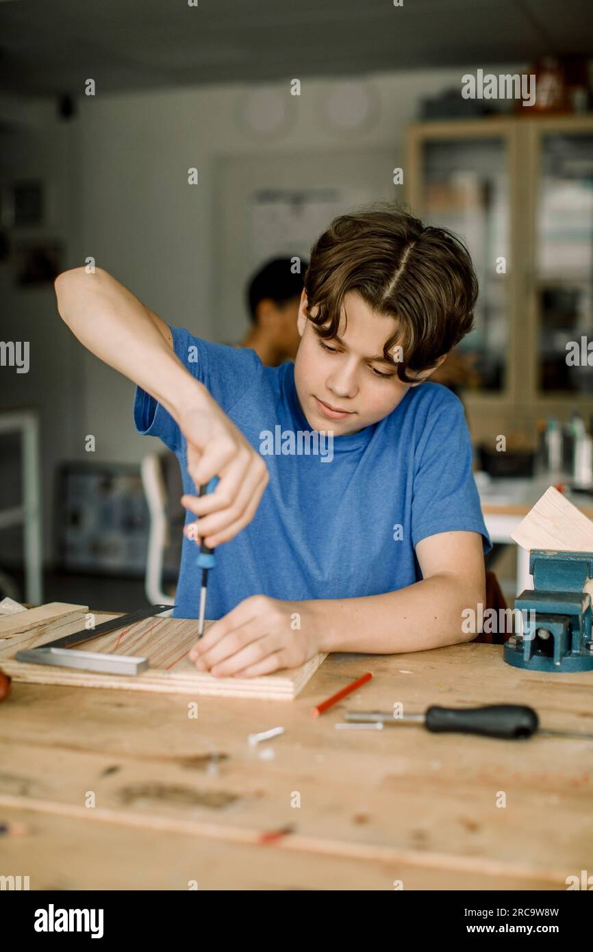 Male teenage student working with screwdriver during carpentry class at ...