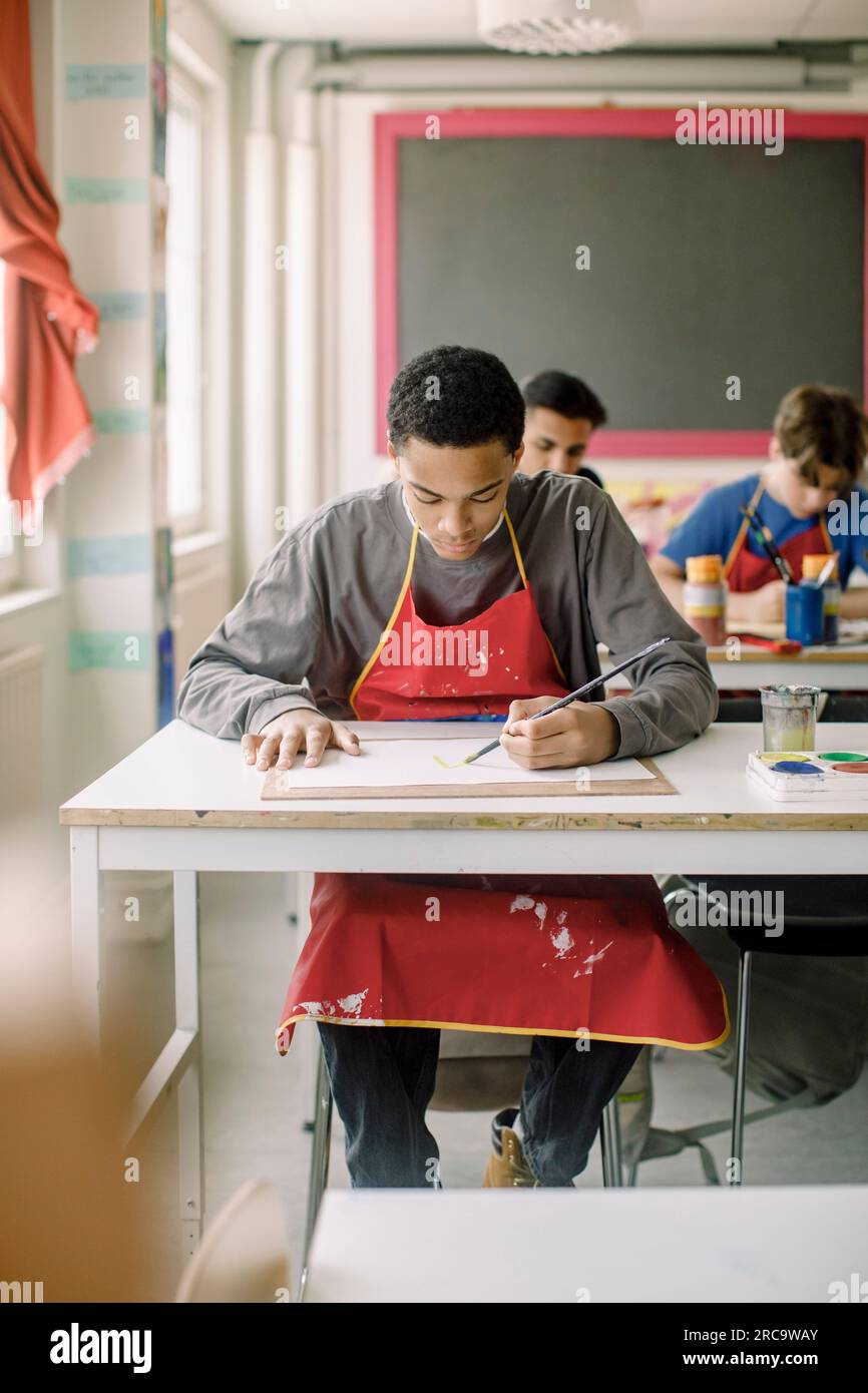 Male teenage student doing artwork during painting class at high school ...