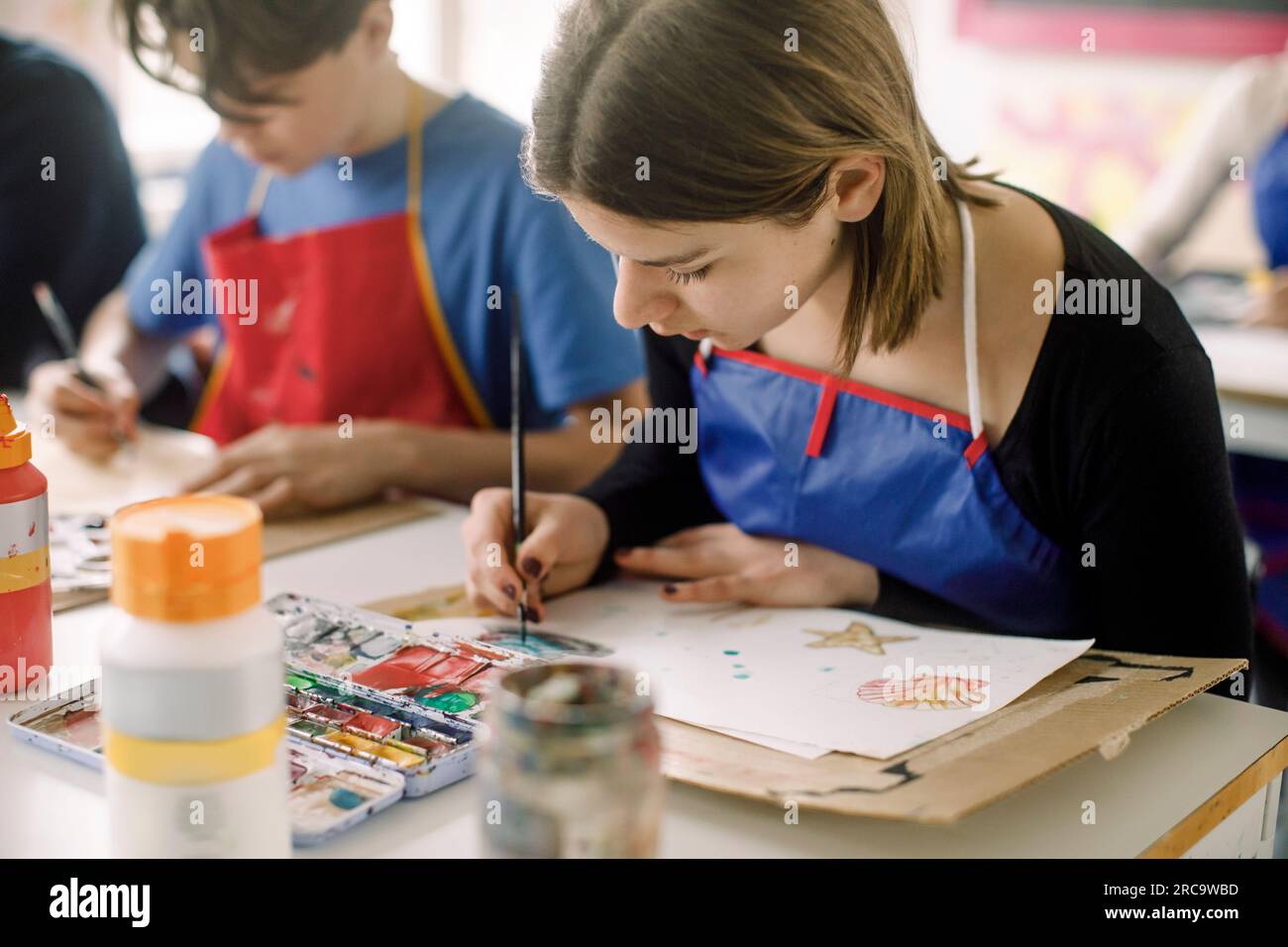 Female teenage student painting with brush during art class at high ...