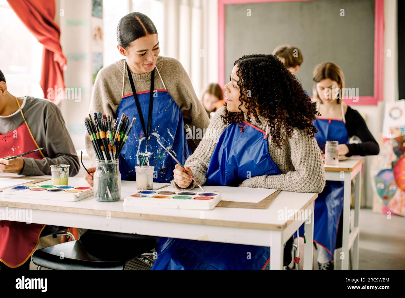 Smiling female teacher assisting teenage student during art class at ...