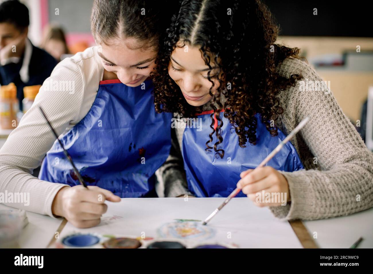 Smiling female teenage students practicing artwork during painting ...