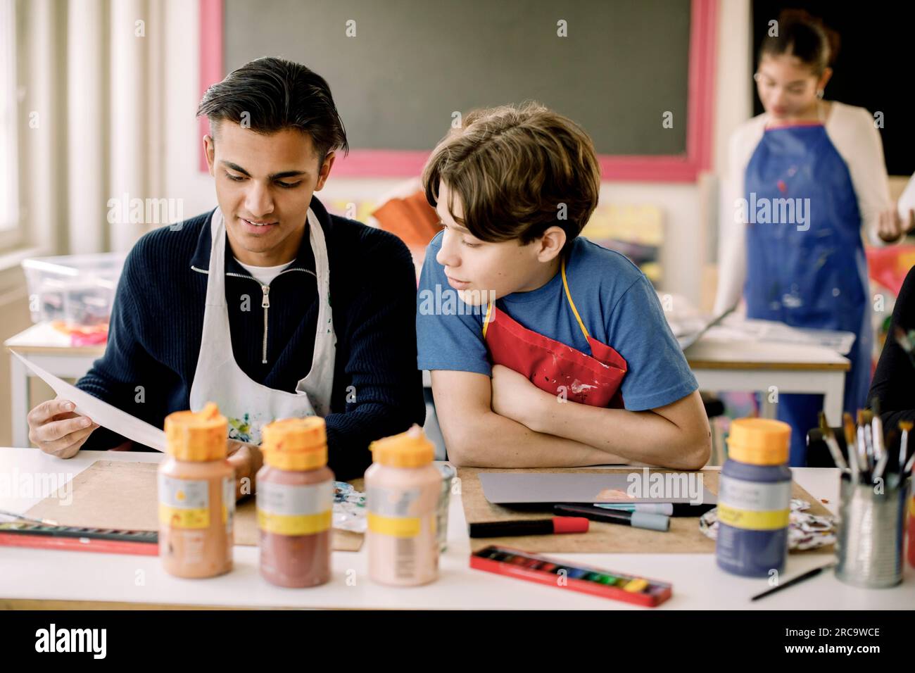 Teenage male student looking at friend's artwork during painting class ...