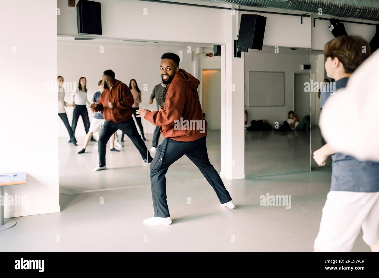 Smiling teacher looking at teenage students practicing dance in studio ...