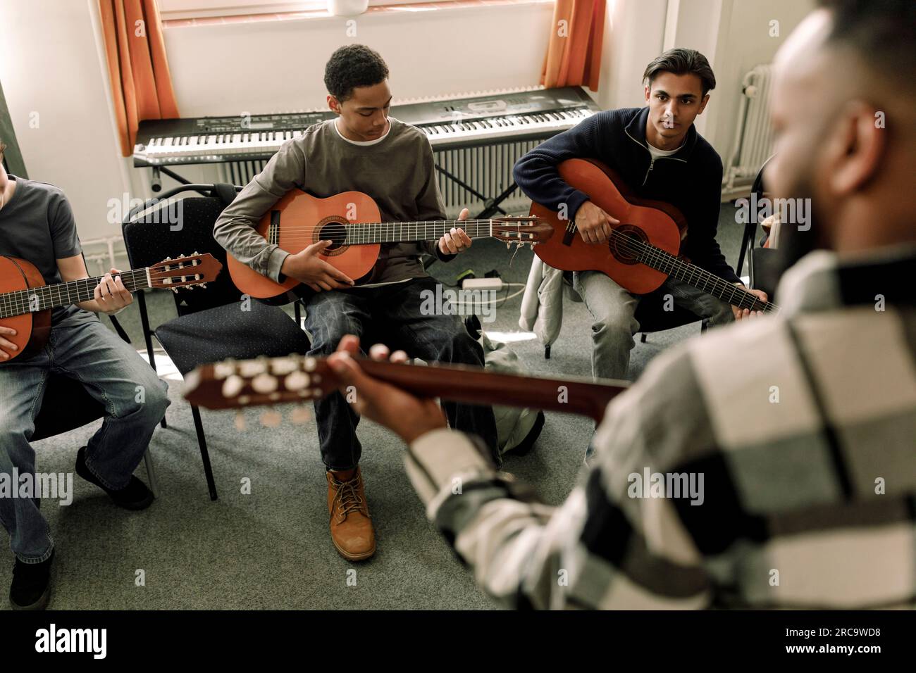 Male teenage students leaning guitar in music class at high school ...