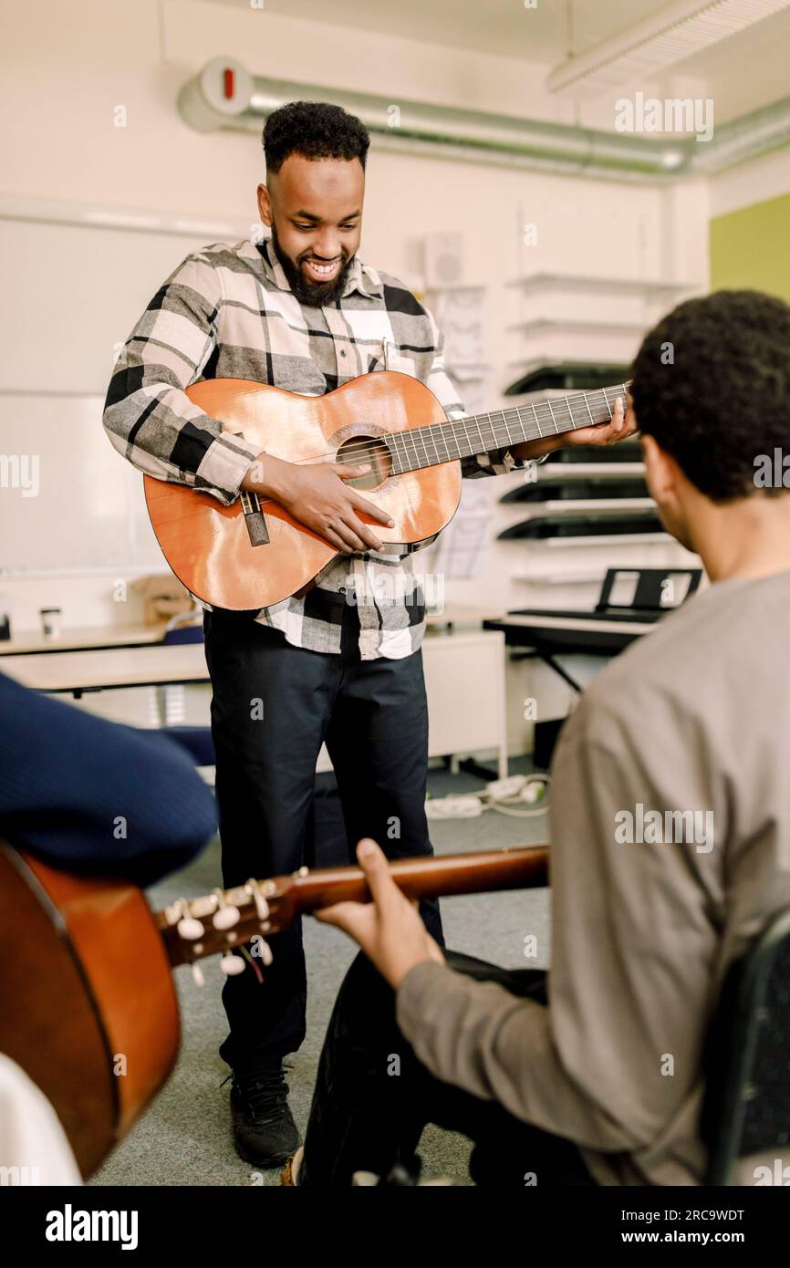 Male teacher playing guitar with students in music class at high school ...