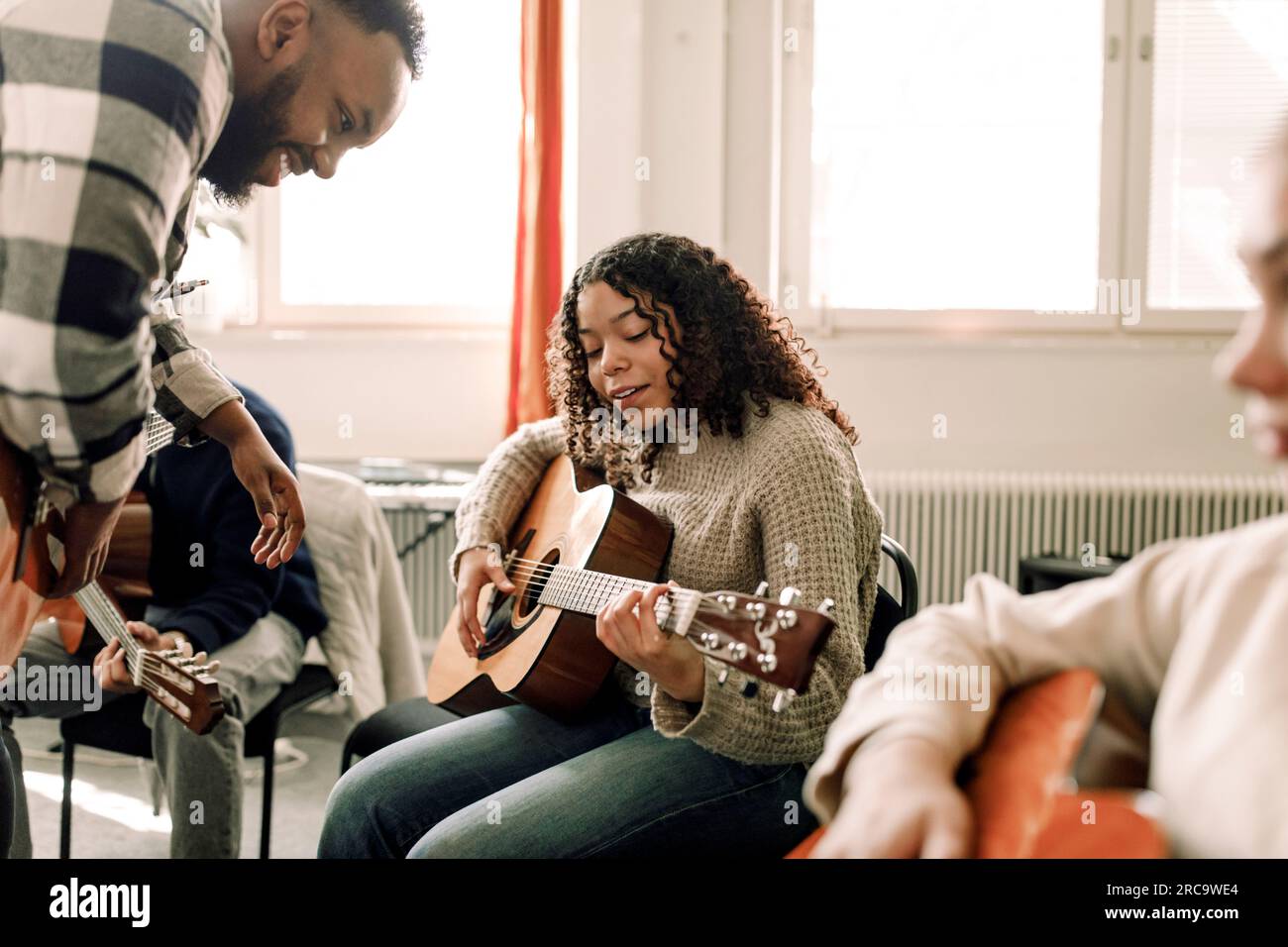 Teenage girl learning to play guitar with male teacher in music class ...