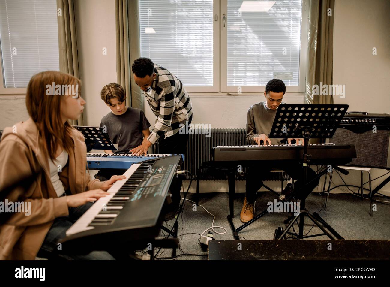 Teacher assisting teenage students during piano class at high school ...