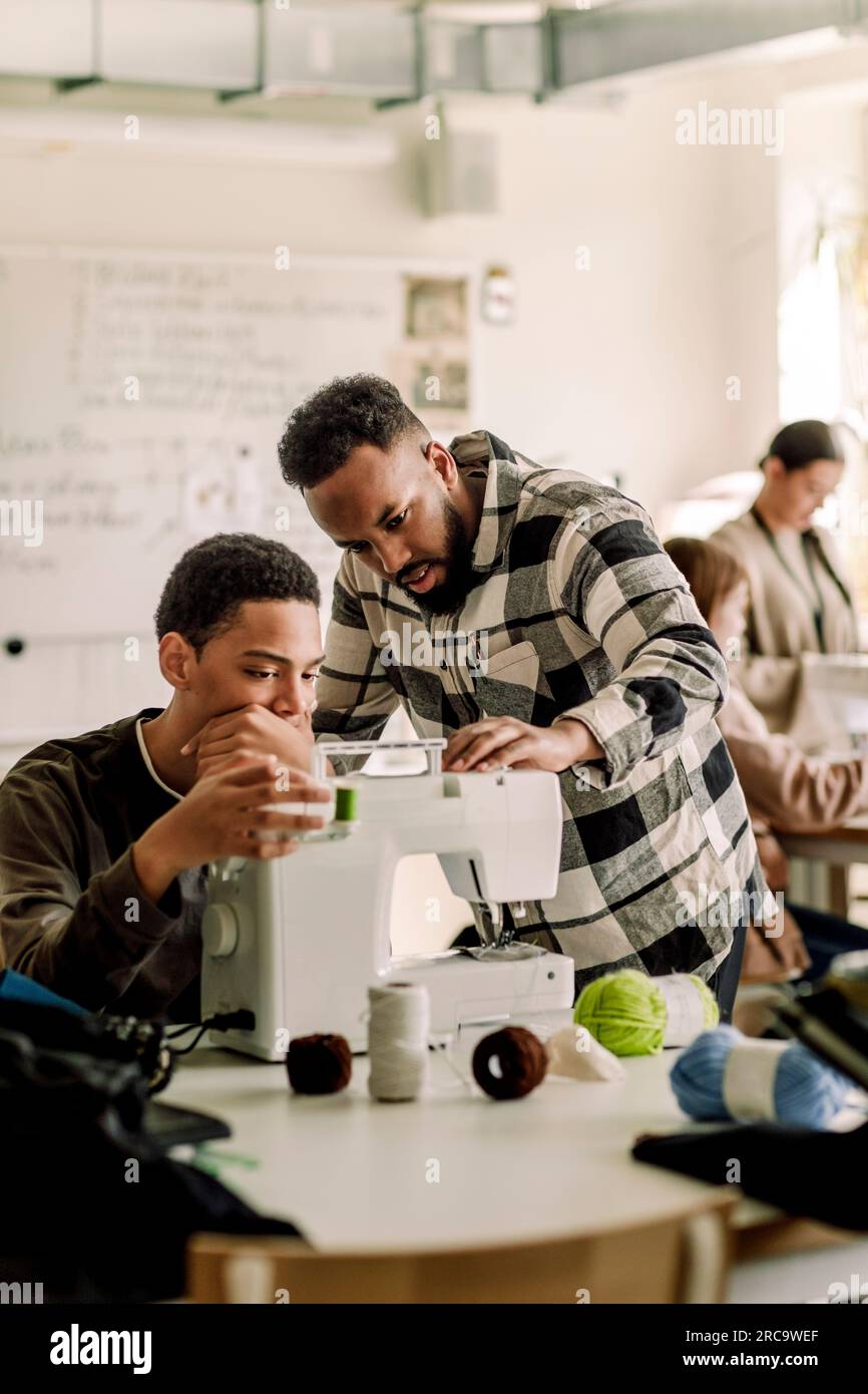Teacher explaining sewing machine to student in art class at high ...