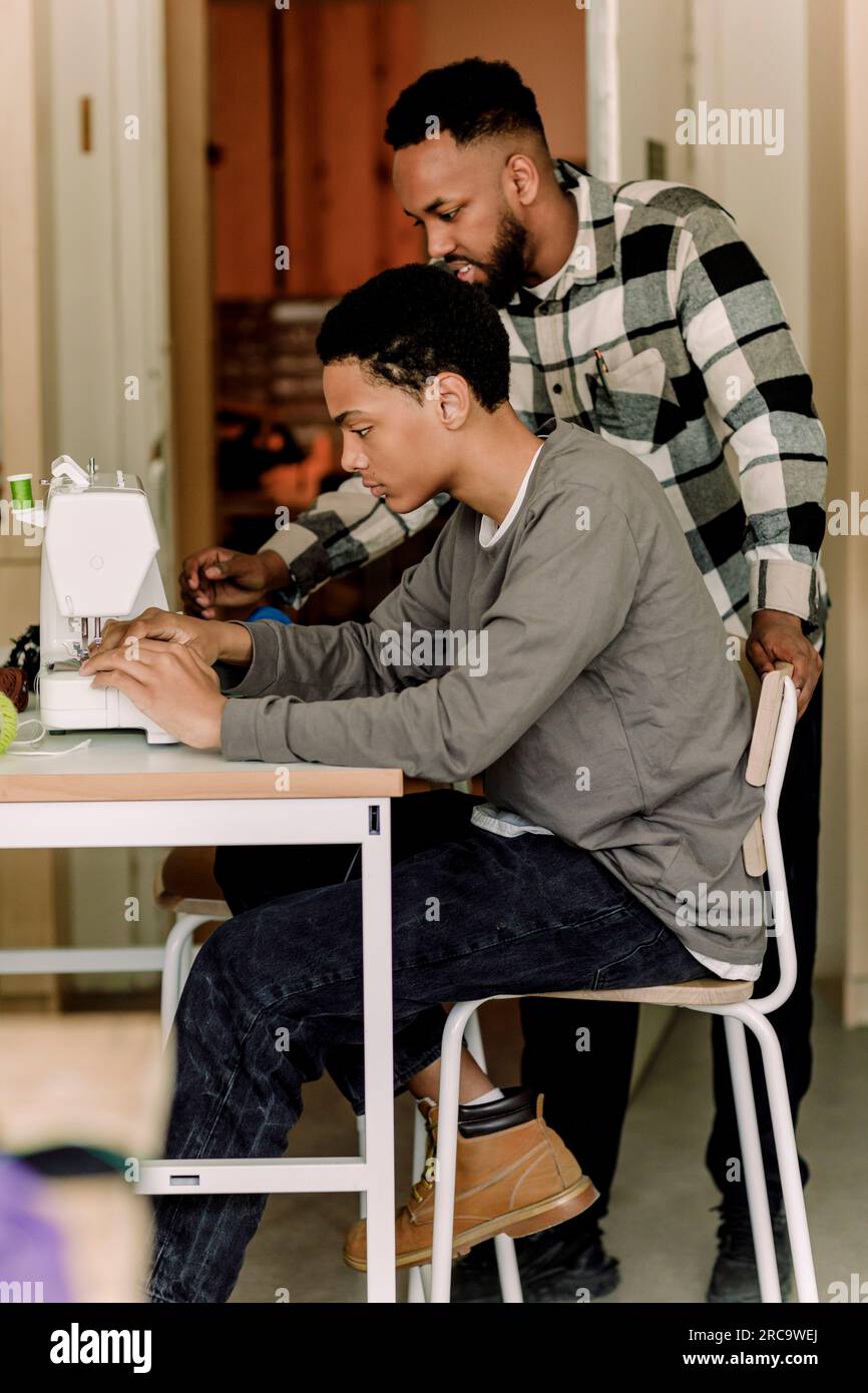 Teenage boy learning stitching using sewing machine by teacher in art ...