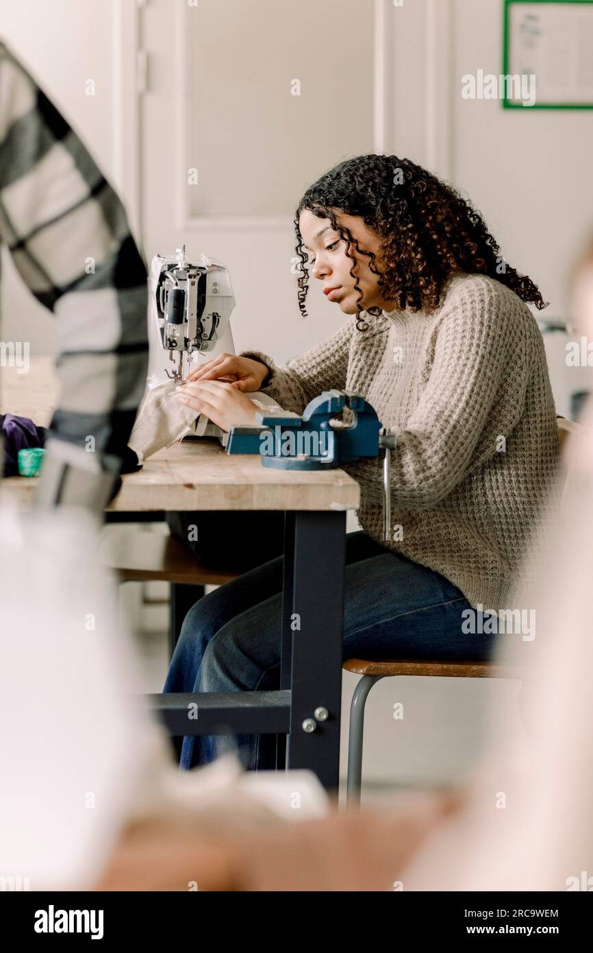 Teenage girl with curly hair using sewing machine in art class at high ...