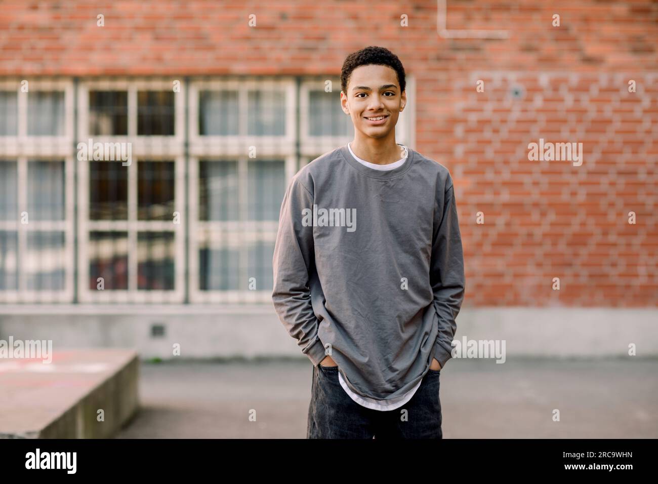 Portrait of smiling male student standing with hands in pockets in high ...